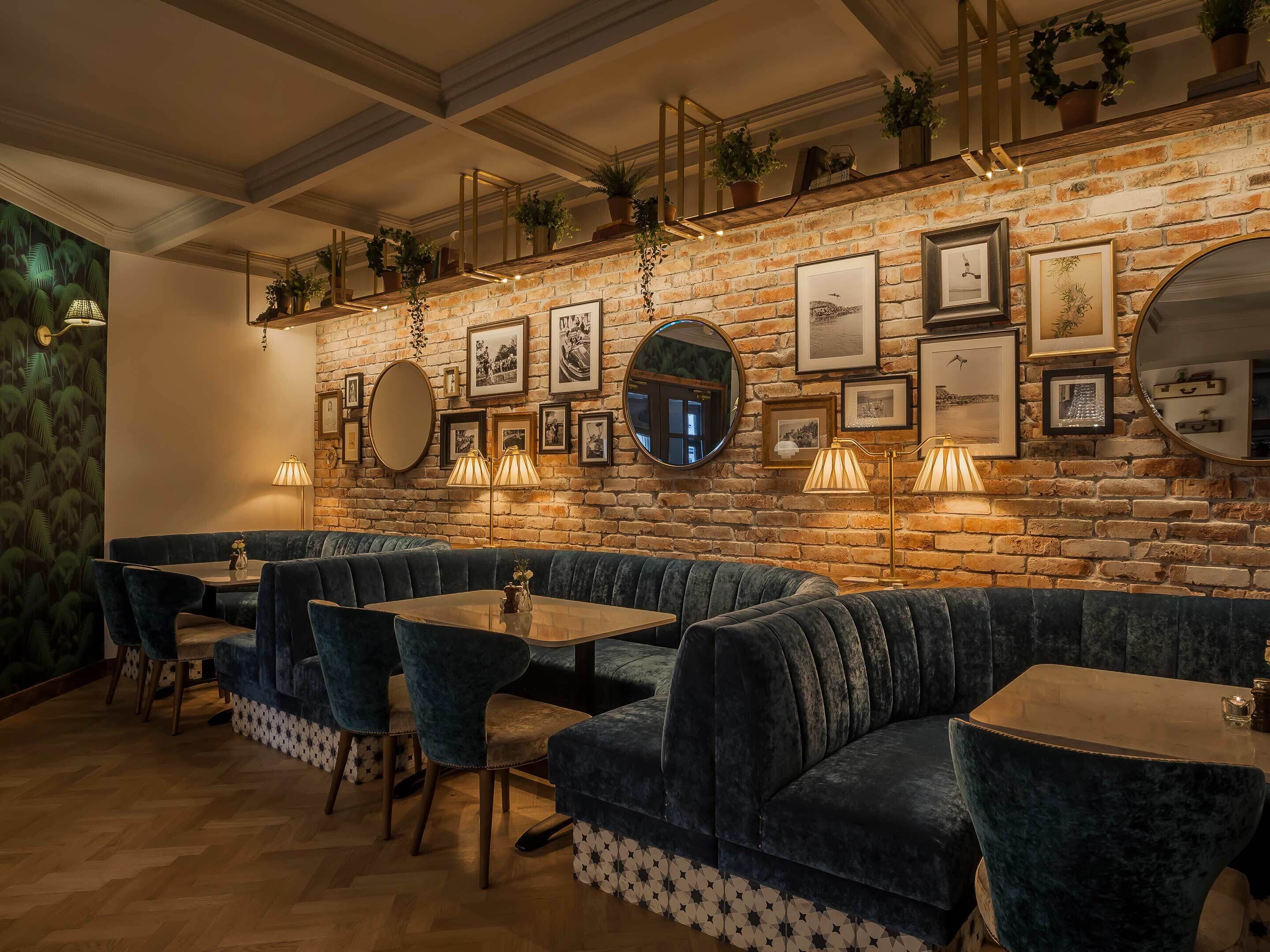 Um restaurante acolhedor com paredes de tijolo, quadros emoldurados e assentos em veludo azul.