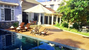 Piscina com espreguiçadeiras e guarda-sóis, parede de pedra e área de pátio com azulejos.