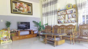 Uma sala de estar com televisão, móveis de madeira, estante de livros e uma planta grande.