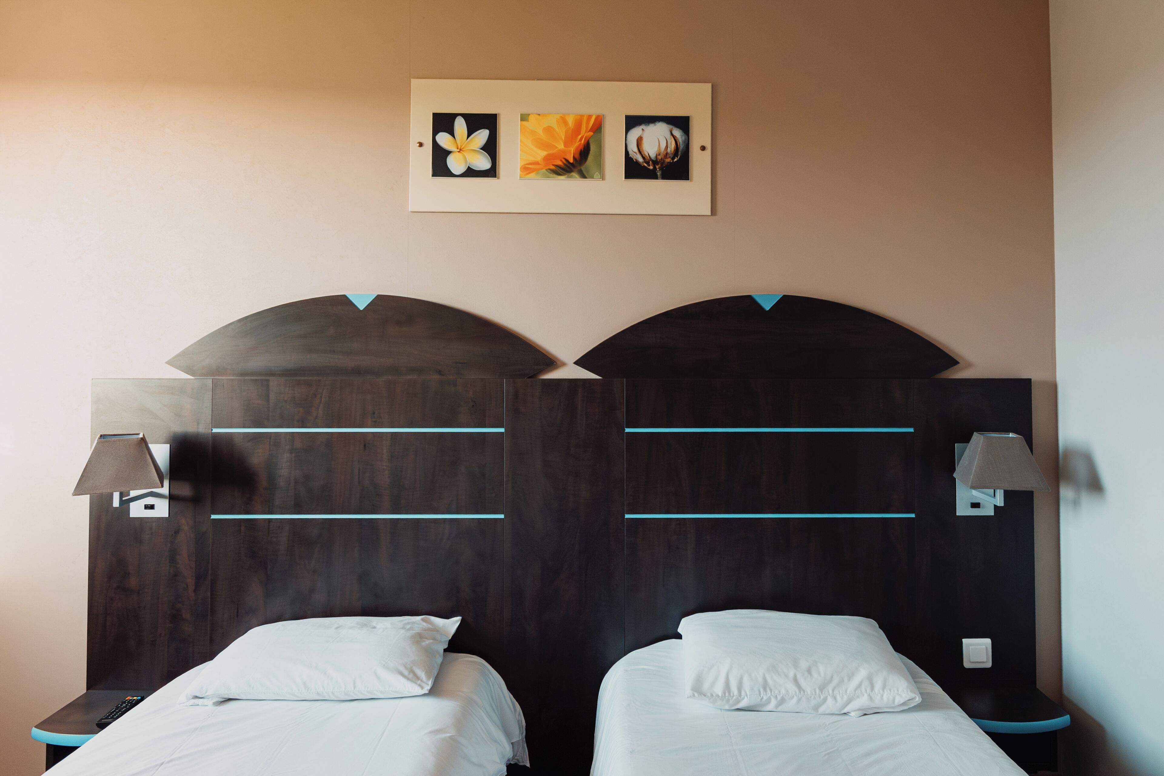 Quarto de hotel com duas camas, cabeceira em madeira escura, abajures e um quadro de flores na parede.
