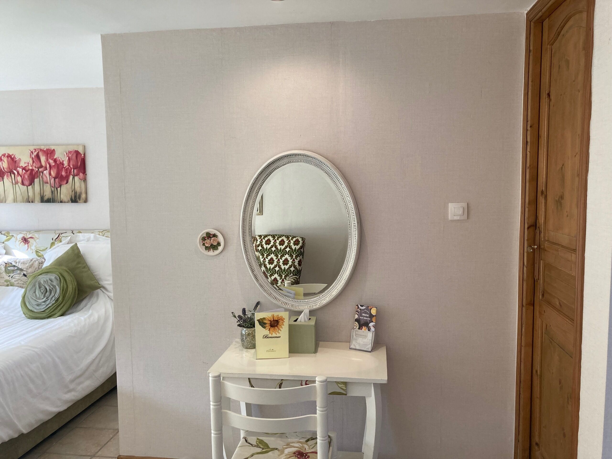 Quarto com cama, cômoda branca com espelho e porta.