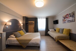Quarto de hotel com duas camas, um banco de madeira, uma televisão e um candeeiro fixado na parede.