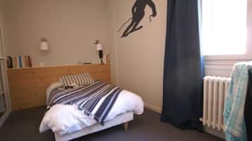 Quarto com cama, luminária na parede, radiador e janela com cortinas.
