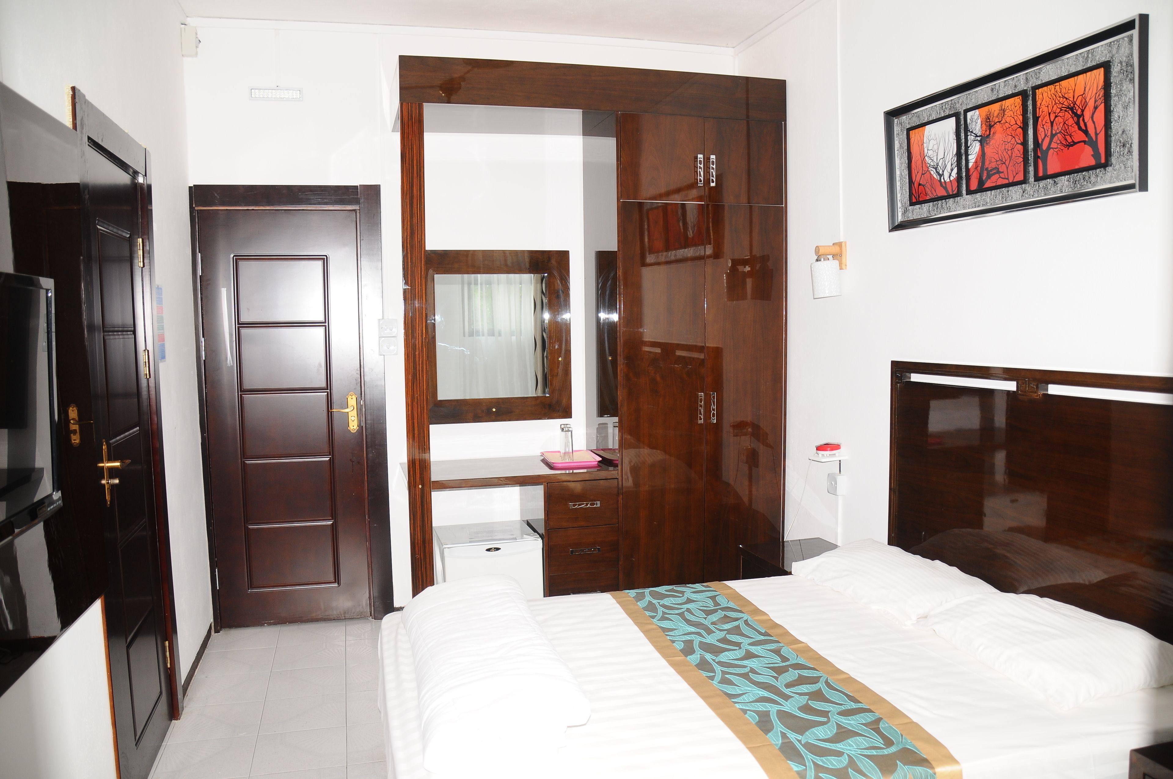 Quarto de hotel com uma cama, um guarda-roupa, uma escrivaninha e um espelho.