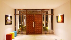 Um interior moderno com uma grande porta de madeira, obras de arte emolduradas e banquetas coloridas.