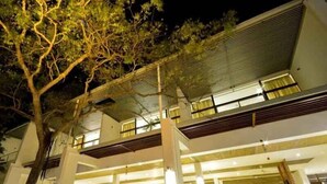 Um edifício moderno com telhado plano, janelas grandes e uma árvore na frente.