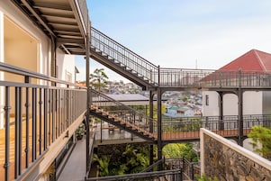 Varanda externa em vários níveis, com grades de metal, parede de pedra e vista para uma área residencial.