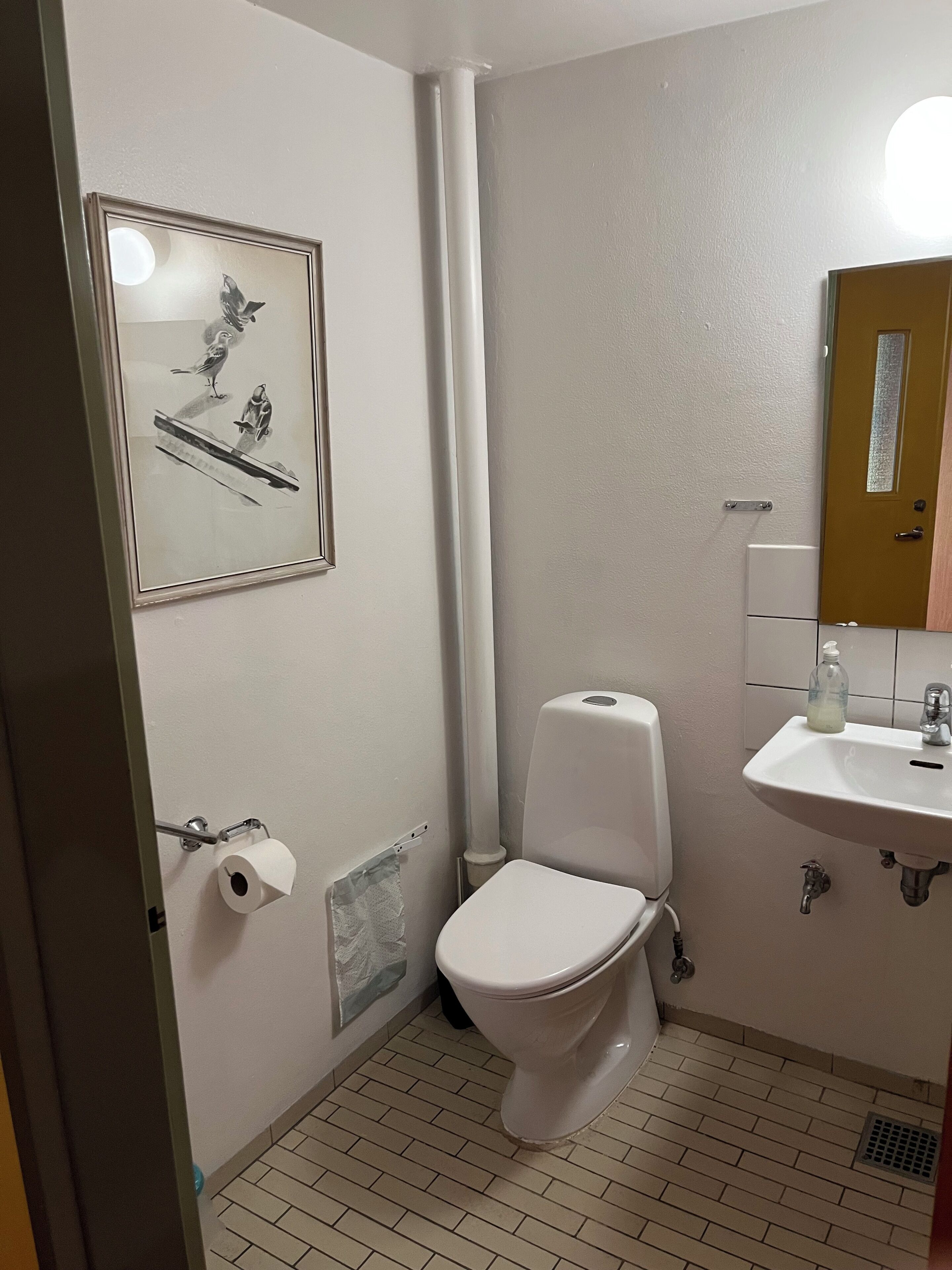 Casa de banho com sanita, lavatório e um quadro emoldurado na parede.