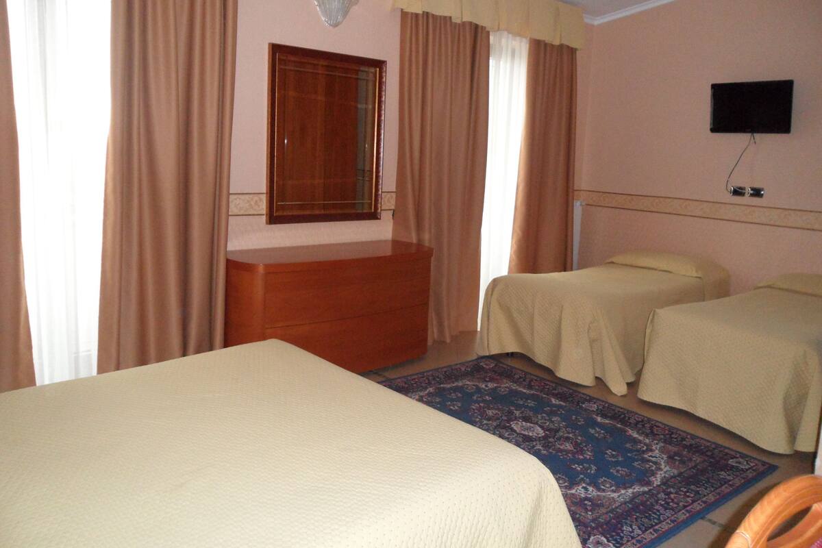 Quarto de hotel com duas camas, cômoda de madeira, televisão na parede e tapete estampado no chão.