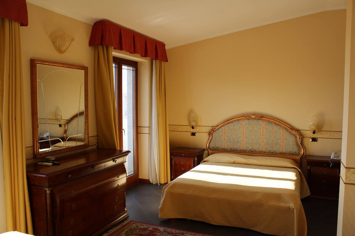 Quarto de hotel com uma cama grande, penteadeira, espelho e janela com cortinas.