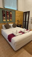 Cama bem arrumada com lençóis brancos e toalhas decorativas, cabeceira de madeira, mesa de cabeceira com abajur e três quadros na parede.