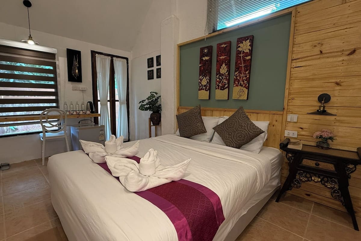 Quarto de hotel com uma cama grande, cabeceira de madeira, mesa de cabeceira com abajur, janela com persianas e uma parede com obras de arte.