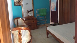 Um quarto com uma cama, cômoda de madeira, uma cadeira, um espelho e um quadro na parede.