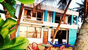 Um edifício de dois andares chamado Mari Gold Beach House, com área de estar à beira-mar, com cadeiras estampadas e uma mesa.