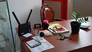 Uma mesa de madeira com um computador, fones de ouvido, uma planta, chaves e alguns papéis.