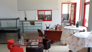 Uma área de refeições com cadeiras vermelhas e pretas, uma mesa com toalha de mesa florida e um aviso de uso exclusivo para funcionários na porta.