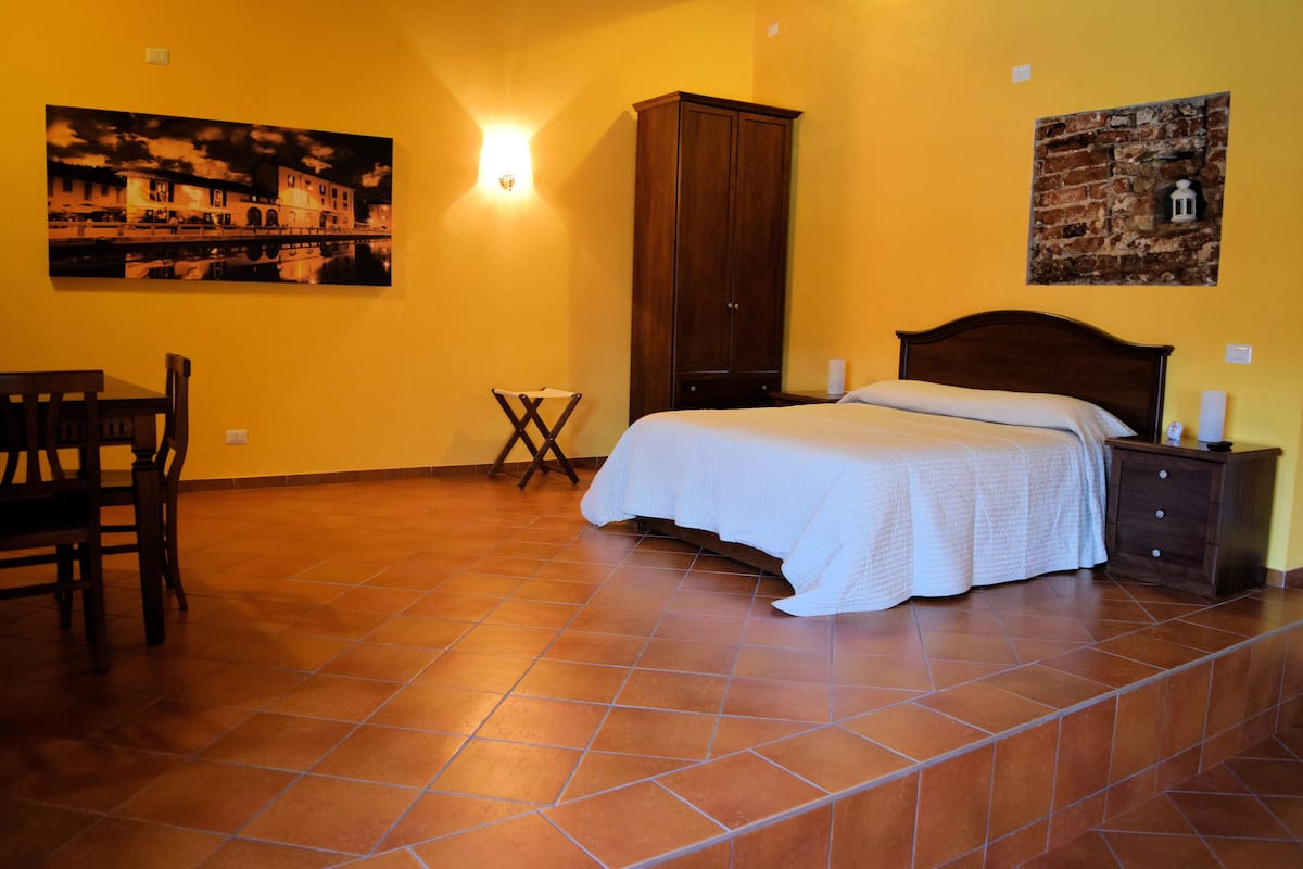 Quarto com cama, guarda-roupa de madeira e mesa de jantar com cadeiras.
