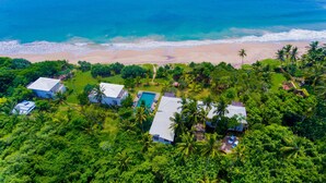 Vista aérea de um resort com várias construções em estilo bungalow, uma piscina e uma praia ao fundo.
