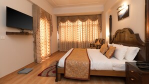Quarto com cama, televisão na parede, penteadeira de madeira e janela com cortinas.