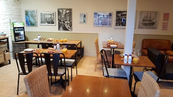 Uma área de refeições com mesas, cadeiras, itens de café da manhã e uma geladeira.