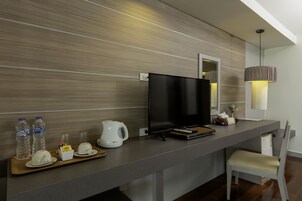 Quarto de hotel moderno com televisão de tela plana, cafeteira e bandeja com garrafas de água e copos.