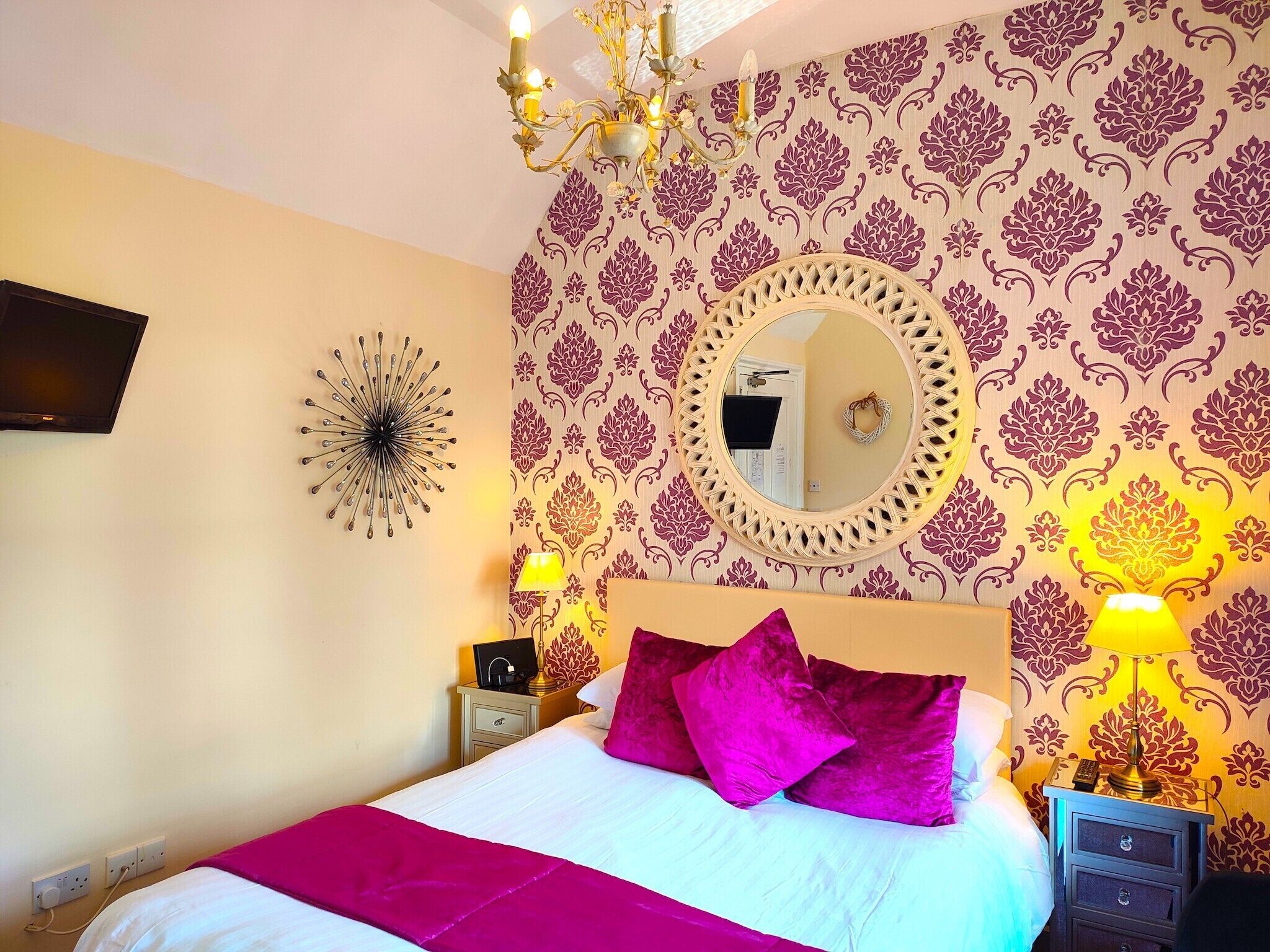 Quarto com cama, espelho, lustre e papel de parede estampado.