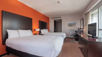 Quarto de hotel com duas camas, uma escrivaninha, uma cadeira e uma janela grande.