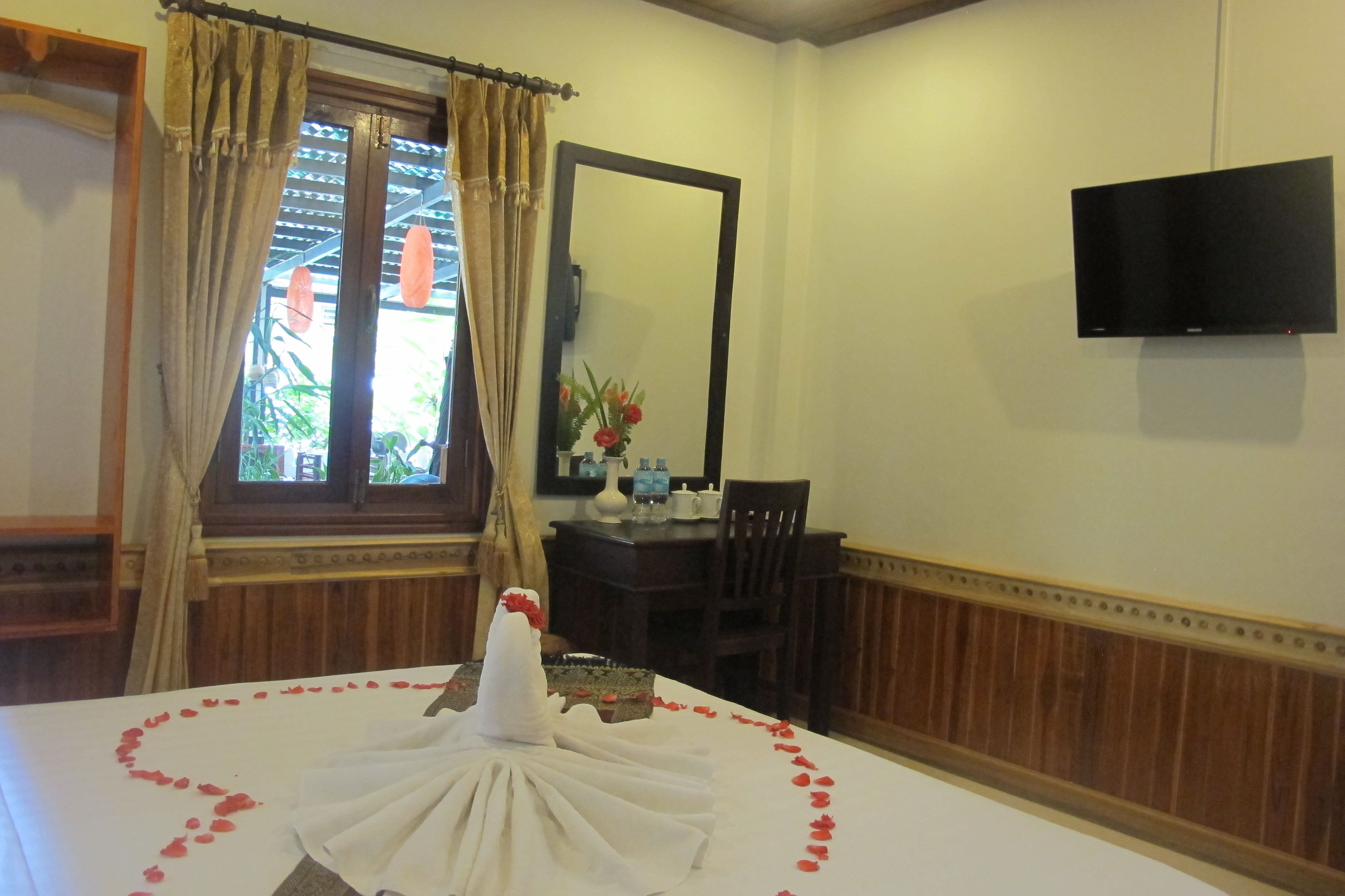 Quarto de hotel com cama, escrivaninha, cadeira, televisão e janela com cortinas.