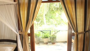 Quarto com cama, cortinas e plantas em vasos numa varanda.