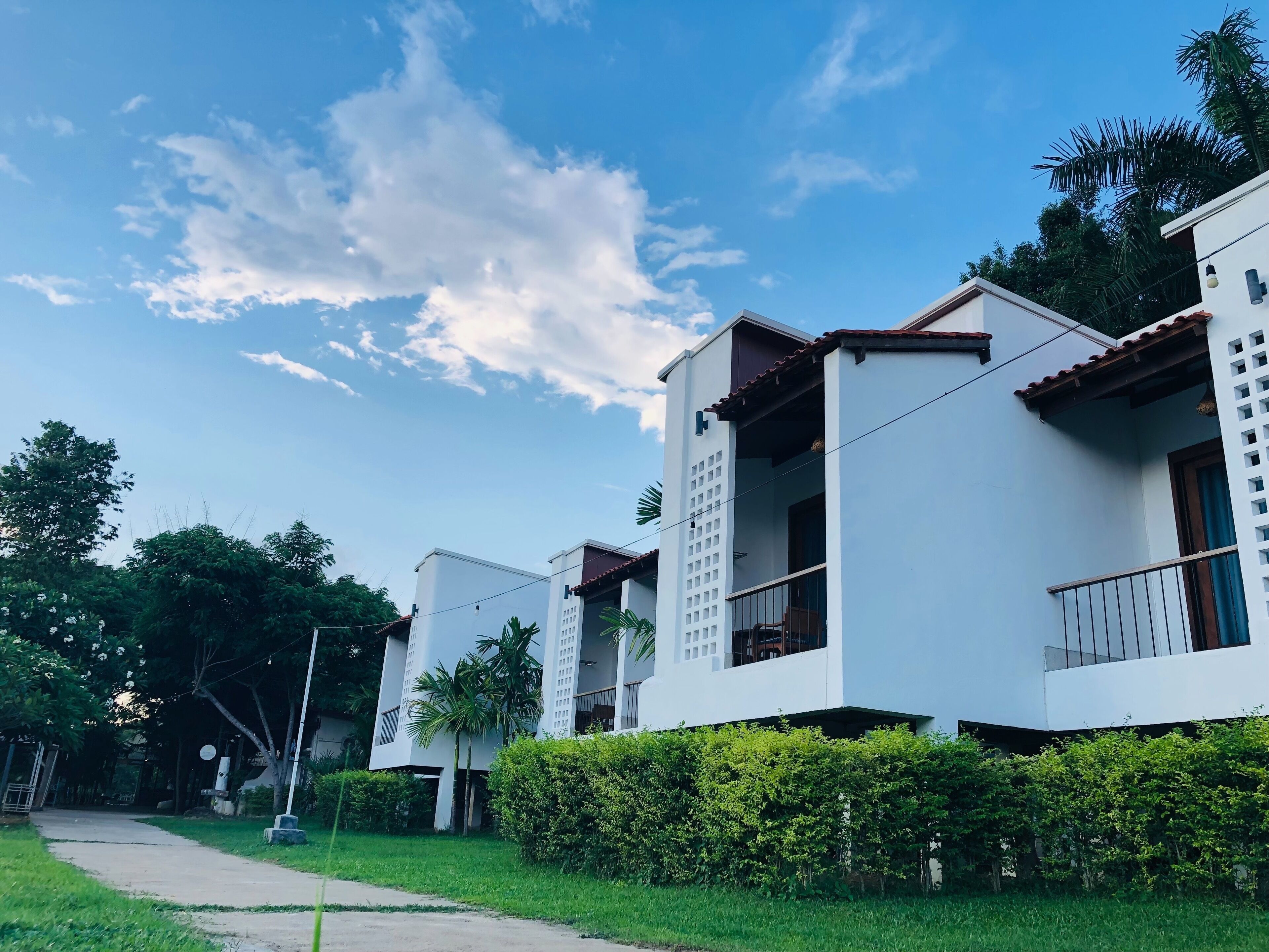 Um edifício residencial moderno com telhado plano, paredes externas brancas e uma varanda com guarda-corpo de metal.