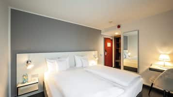 Quarto de hotel com uma cama grande, mesas de cabeceira, um espelho e uma escrivaninha com abajur.