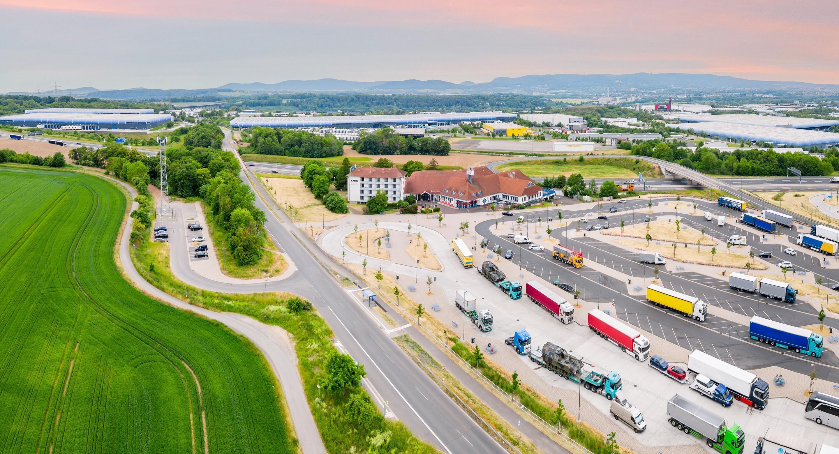 Área industrial com caminhões grandes, um cruzamento rotatório e um edifício com telhado vermelho.