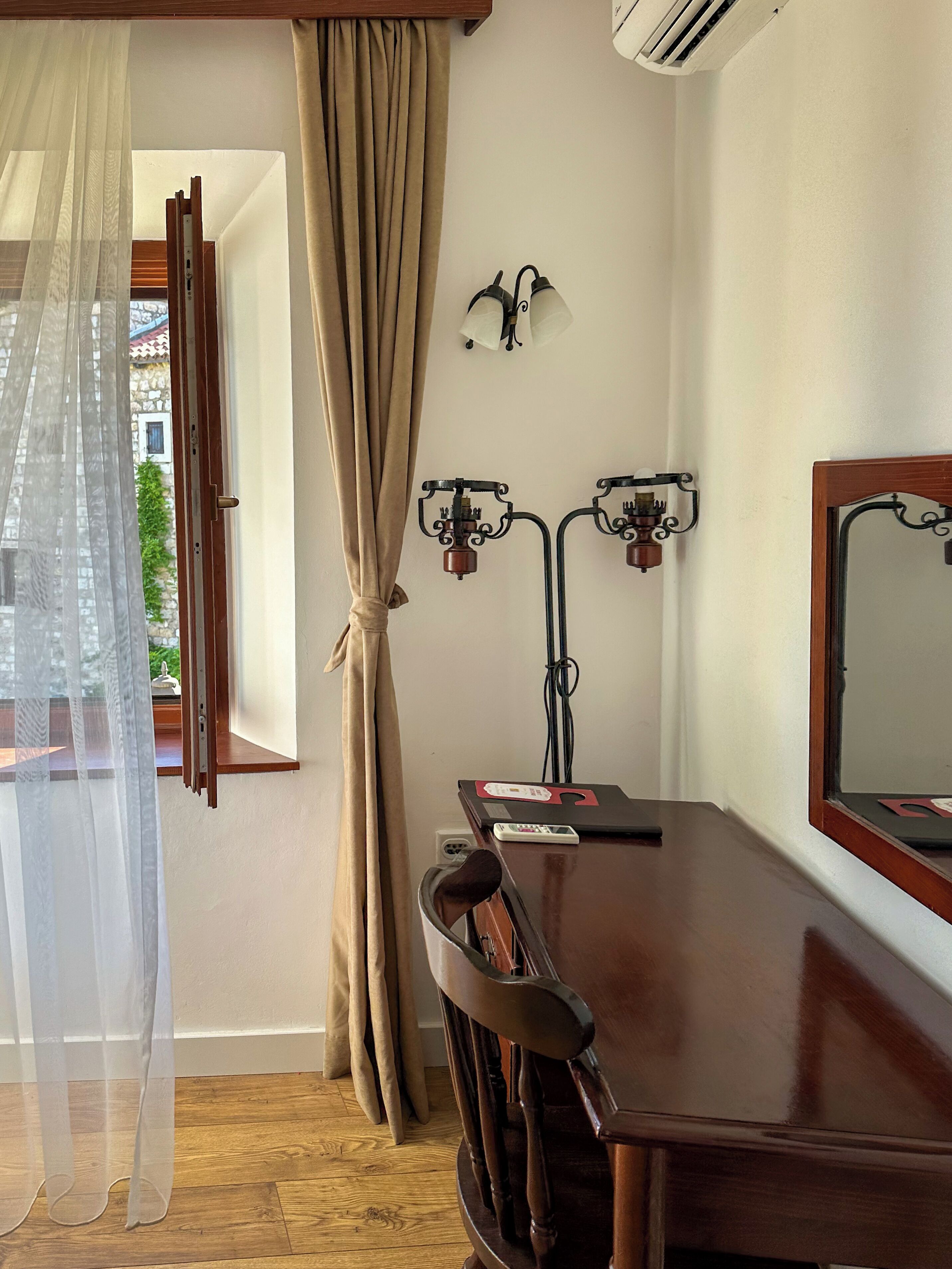 Quarto com mesa de jantar de madeira, uma cadeira, janela com cortinas e luminárias fixadas na parede.