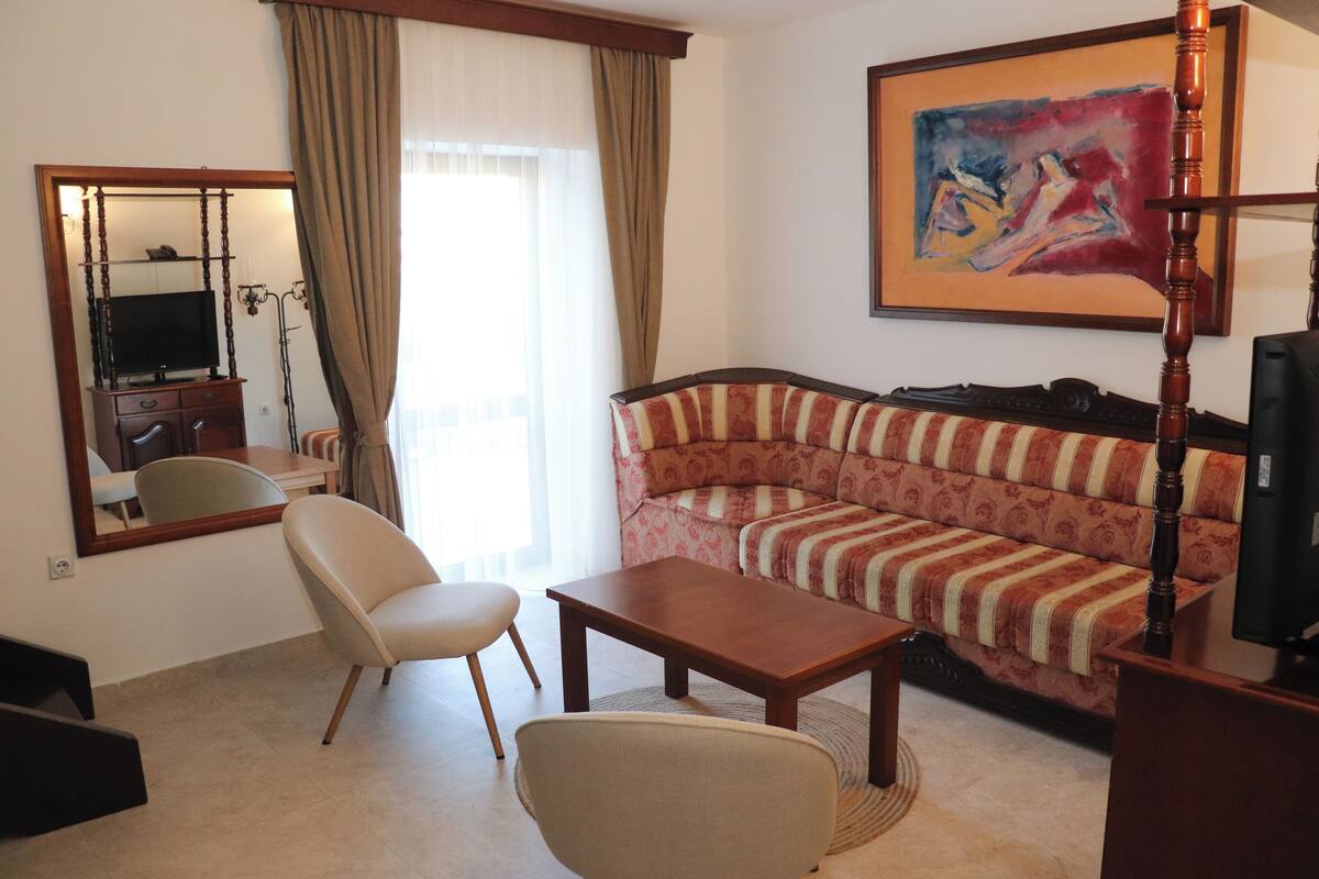 Uma sala de estar com sofá, poltrona, mesa de centro e televisão.