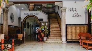 Um hall de hotel com uma escada, um balcão de recepção e uma placa com a inscrição 'Hotel Lolon'.