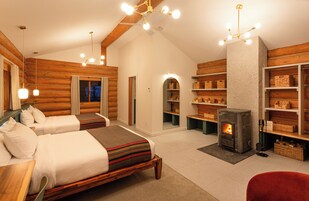 Quarto estilo cabana de tronco com duas camas, lareira, prateleiras de madeira e um ambiente acolhedor.