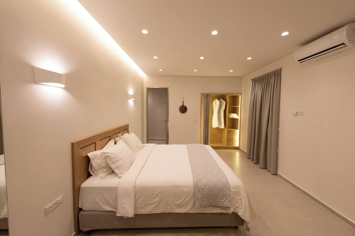 Quarto moderno com cabeceira de madeira, cama com roupa de cama branca, mesa de cabeceira e guarda-roupa.