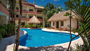Uma área de piscina em resort com piscina azul cristalina, espreguiçadeiras e estruturas de telhado de palha.