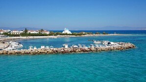 Uma área costeira com um molhe rochoso, barcos e um edifício branco com cúpula azul.