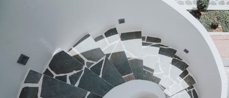 Escadaria em espiral com interior branco e padrão de mosaico no chão.