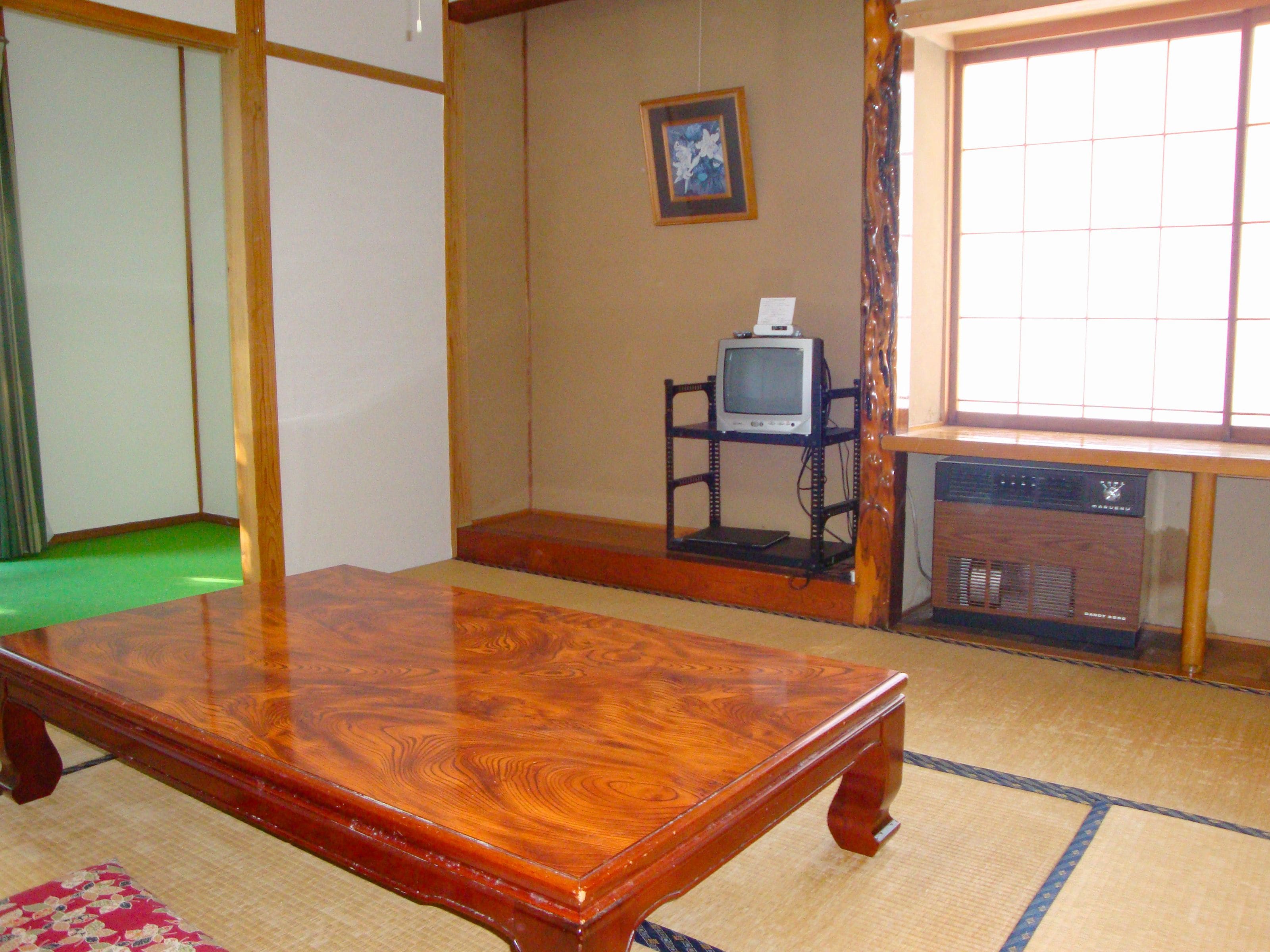 Quarto em estilo japonês tradicional, com tatames, uma mesa de madeira, televisão sobre suporte e aquecedor.