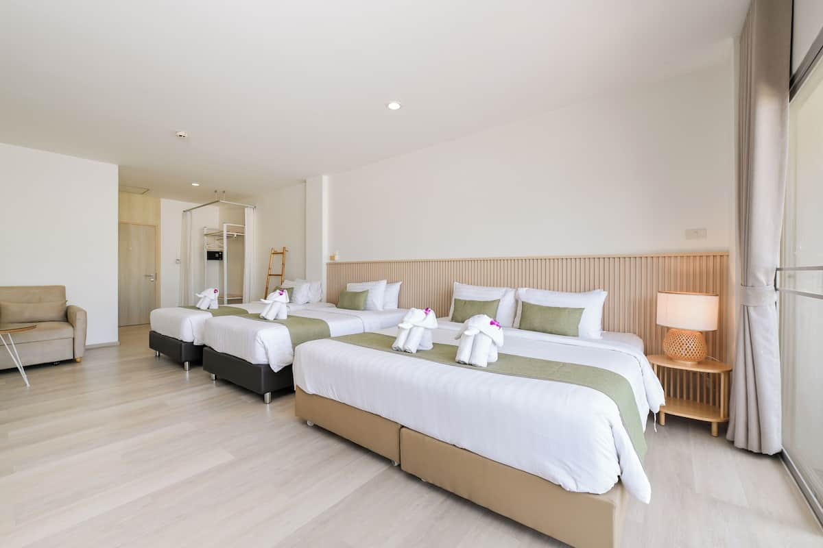 Quarto de hotel com três camas, um sofá, um abajur e um guarda-roupa.