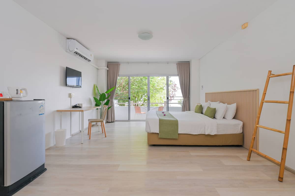 Quarto de hotel moderno com cama, escrivaninha, ar condicionado e vista para o verde lá fora.