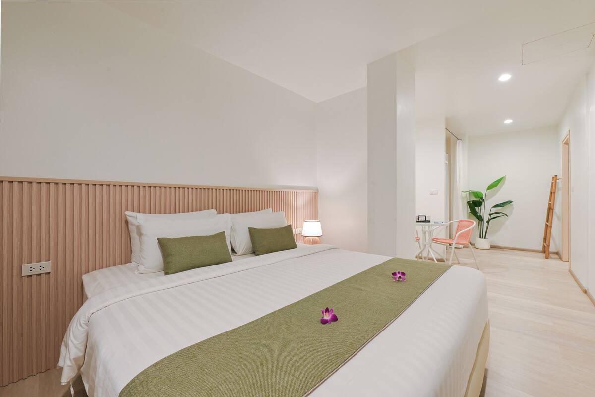 Quarto de hotel com cama, mesa de cabeceira, abajur, cadeira e planta em vaso.