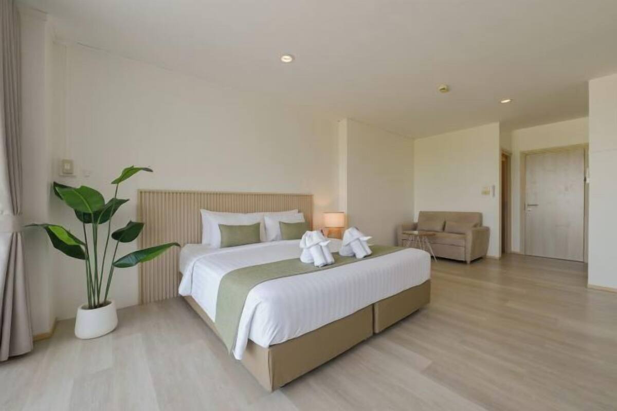 Quarto de hotel com cama, mesa de cabeceira, luminária e planta em vaso.