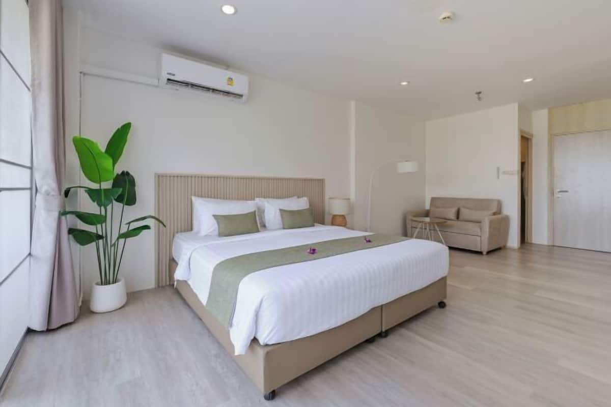 Quarto de hotel moderno com uma cama grande, um vaso de planta, um sofá e uma porta.