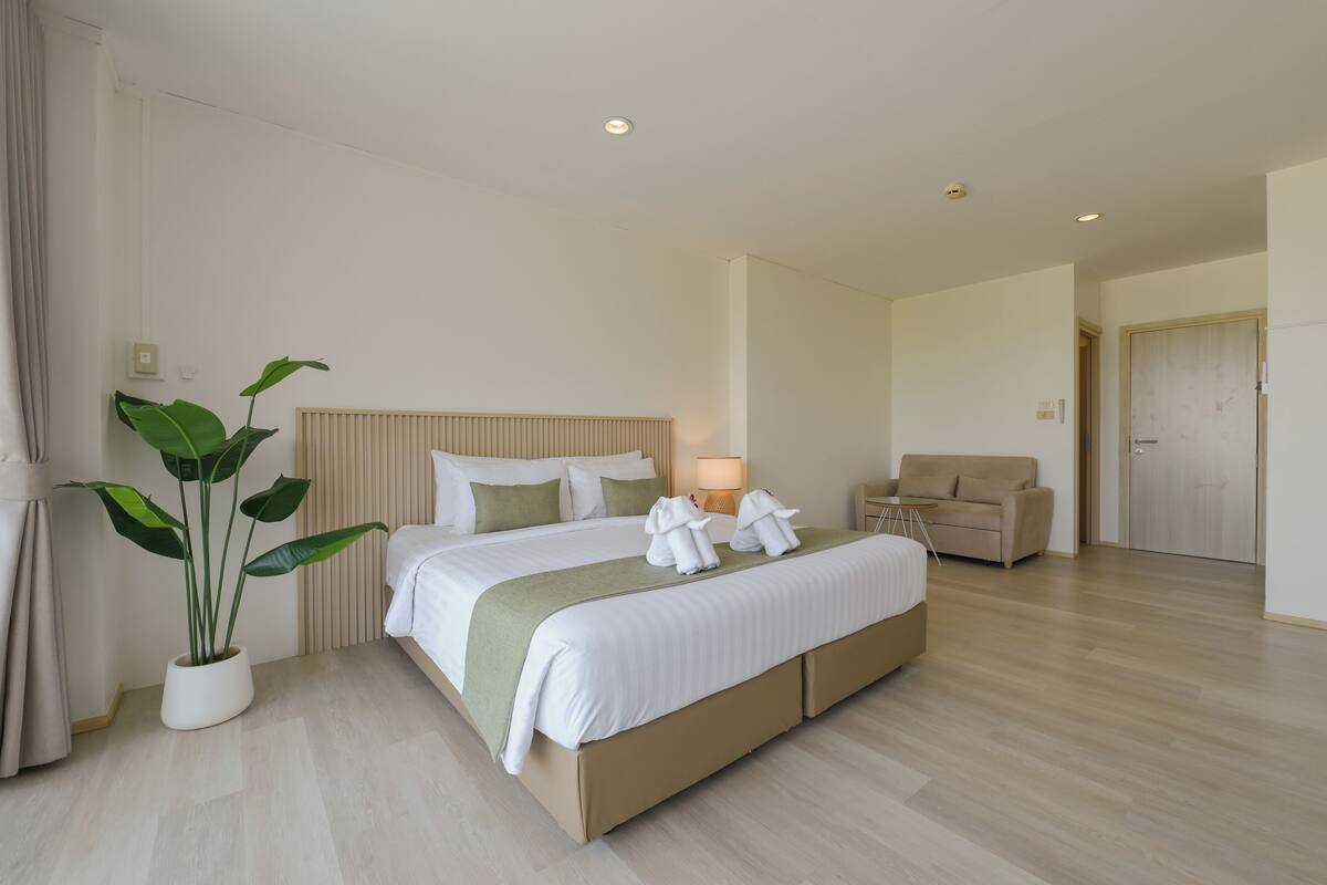 Quarto de hotel com uma cama, um sofá, uma planta em vaso e uma porta.