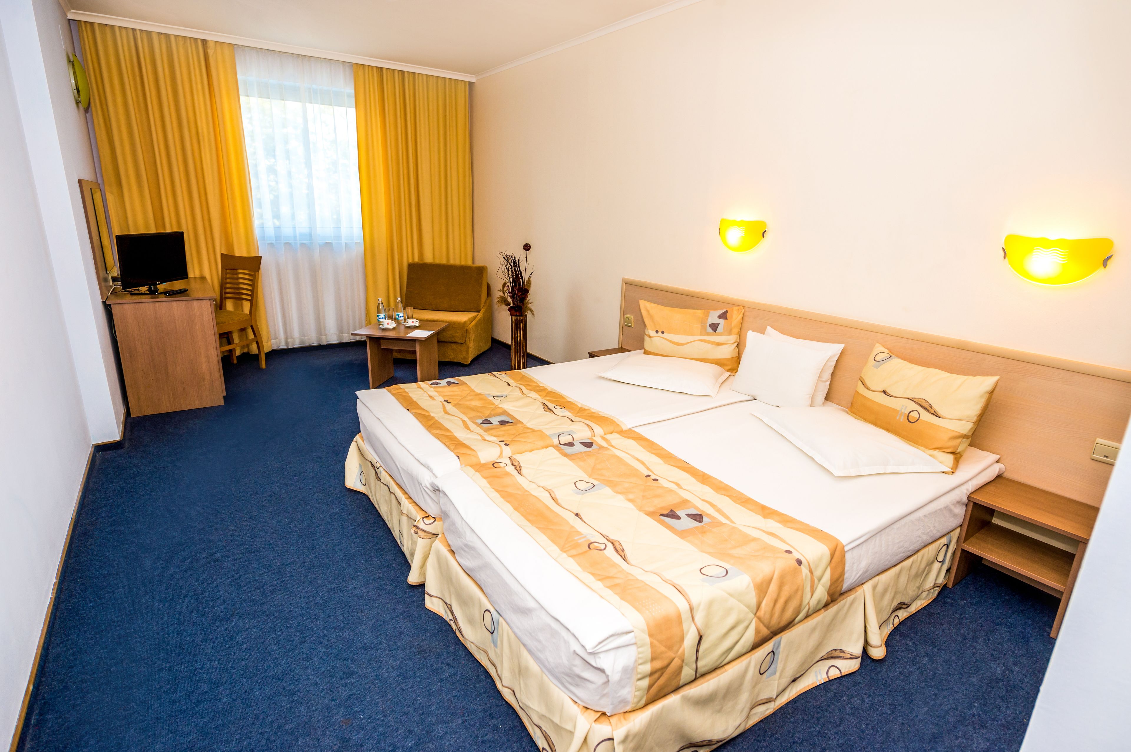 Quarto de hotel com uma cama grande, uma escrivaninha com computador, uma cadeira e uma mesinha.