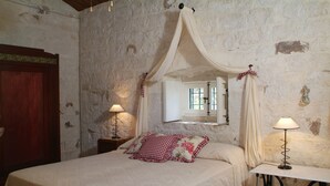 Um quarto com cama, mesa de cabeceira, abajur, espelho e porta de madeira.