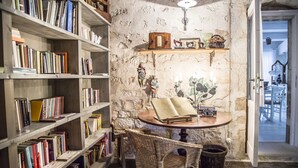 Um cantinho aconchegante para leitura, com estantes, uma cadeira de vime e uma mesa com um livro aberto.
